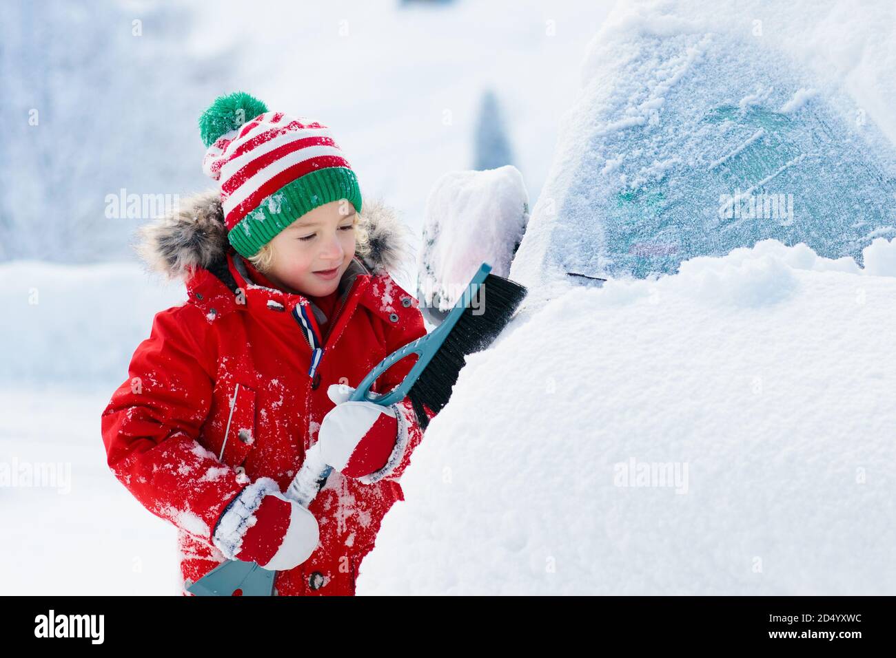Child brushing snow off car after storm. Kid with winter brush and ...