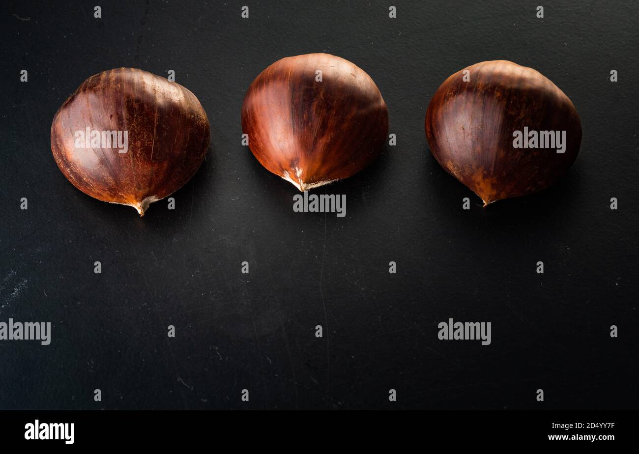 Three chestnuts isolated on black background Stock Photo - Alamy