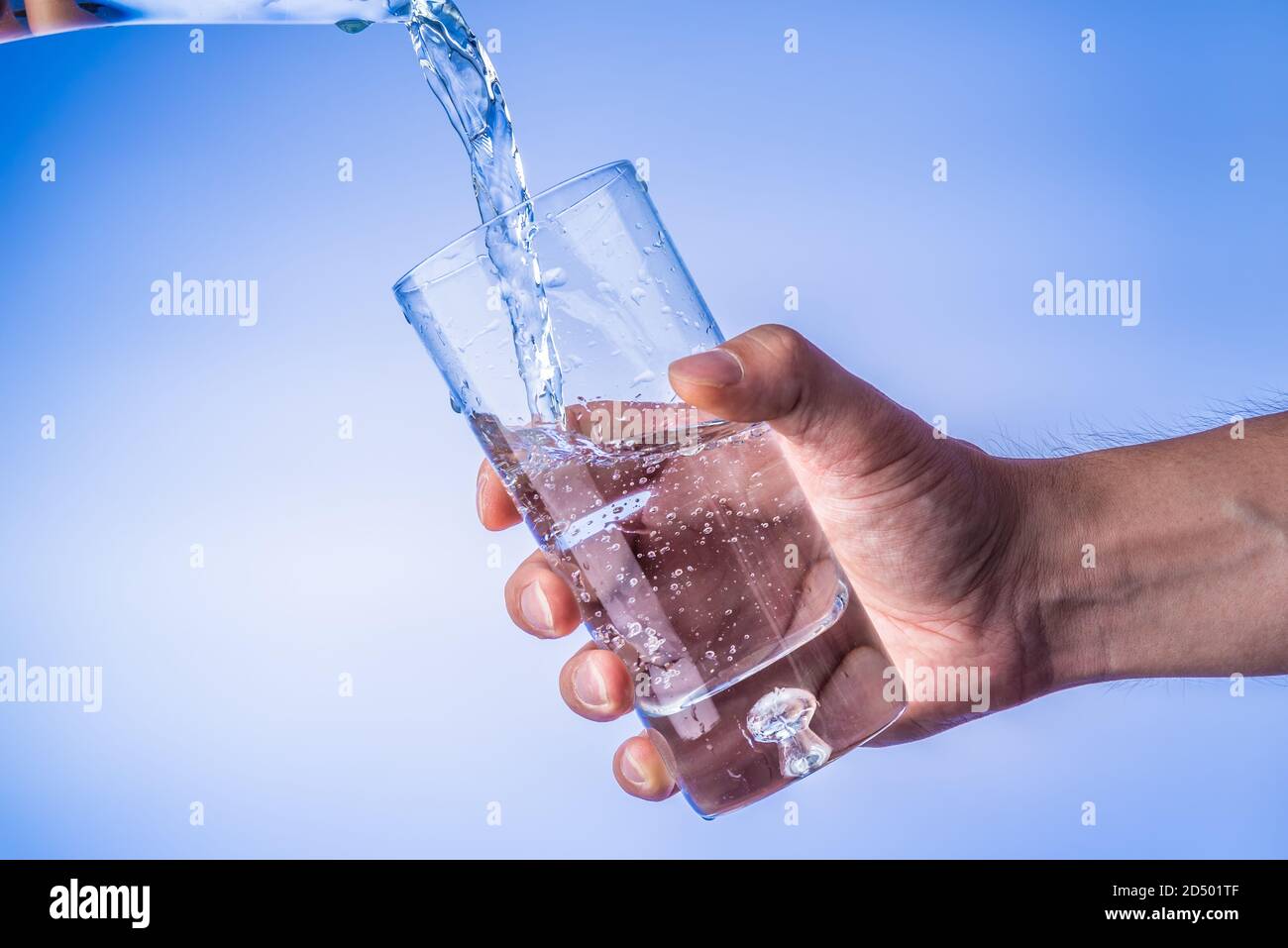 Filling up the glass with water, hand holding glass against bright blue ...