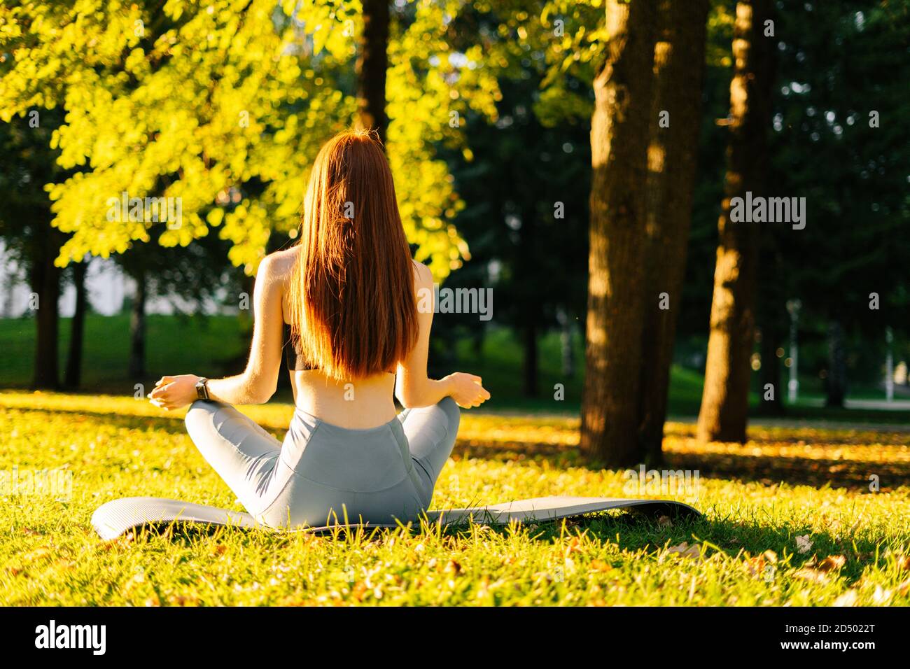 Rear view of slim young redhead woman meditating in lotus pose holding ...