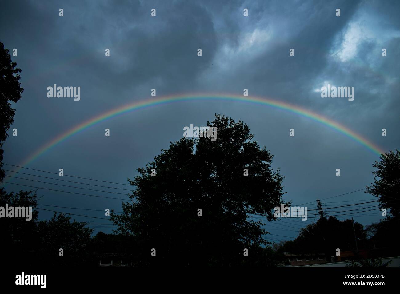 Full rainbow with a dark grey cloudy sk Stock Photo - Alamy