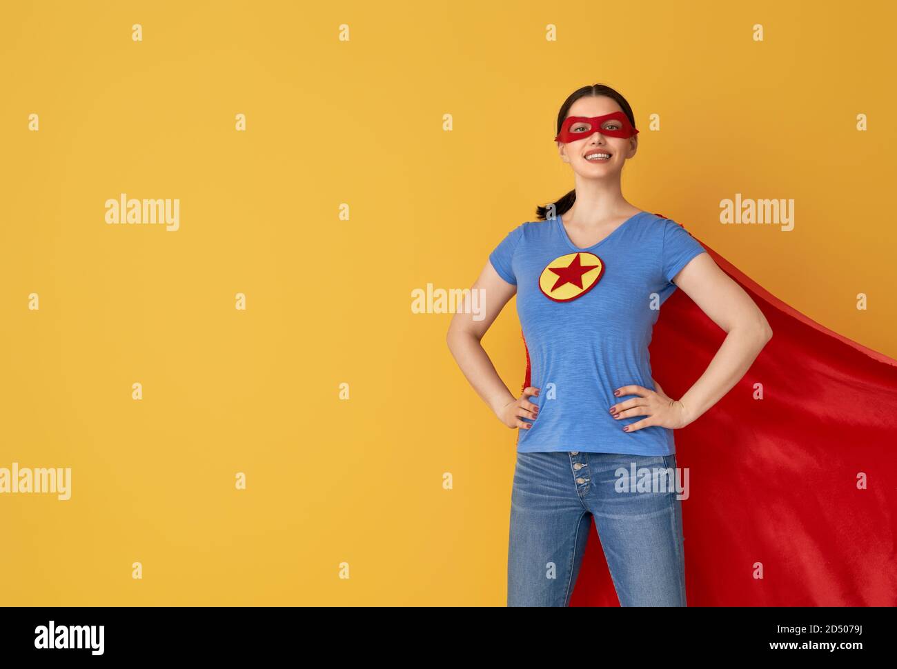 Joyful beautiful young woman in superhero costume posing on yellow ...