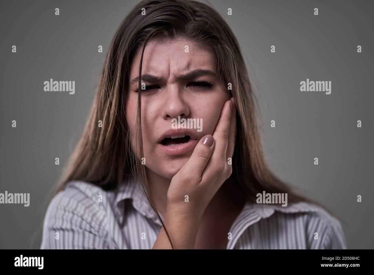 Studio shot of a young woman having a severe tooth ache with hand on ...
