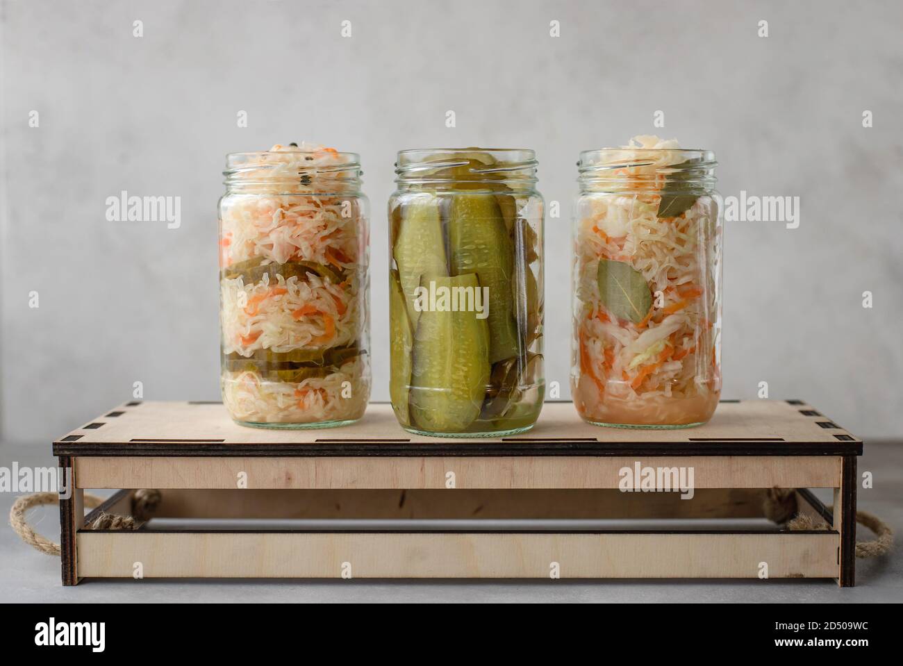 various fermented cabbage and cucumbers in jars on a wooden box. gray ...