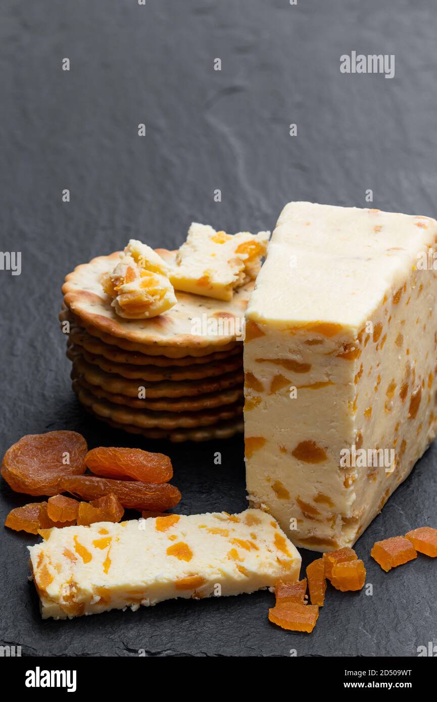 Traditional cheddar cheese with dry apricot on black stone background ...