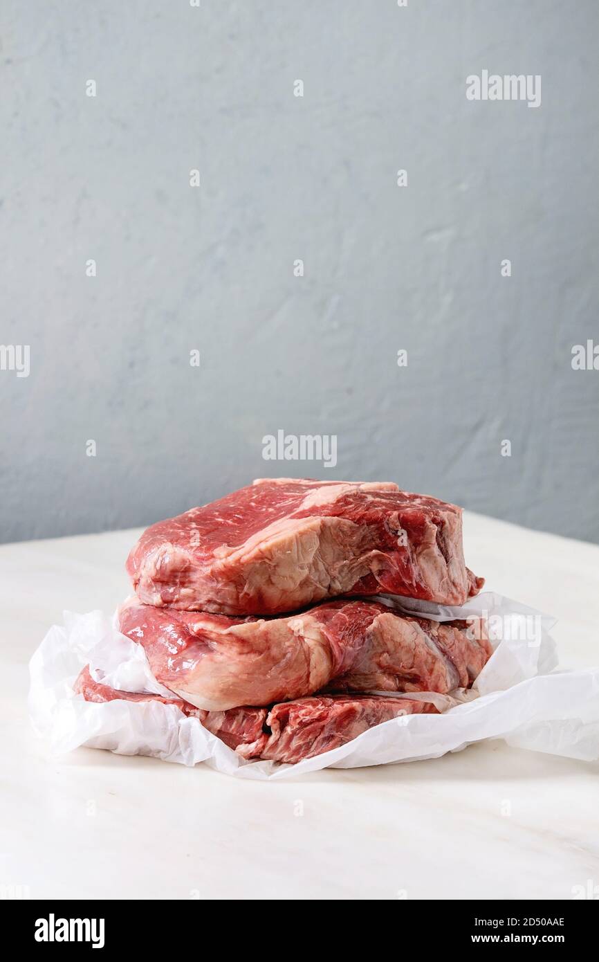 Three raw uncooked beef steaks in stack on crumpled paper on white ...