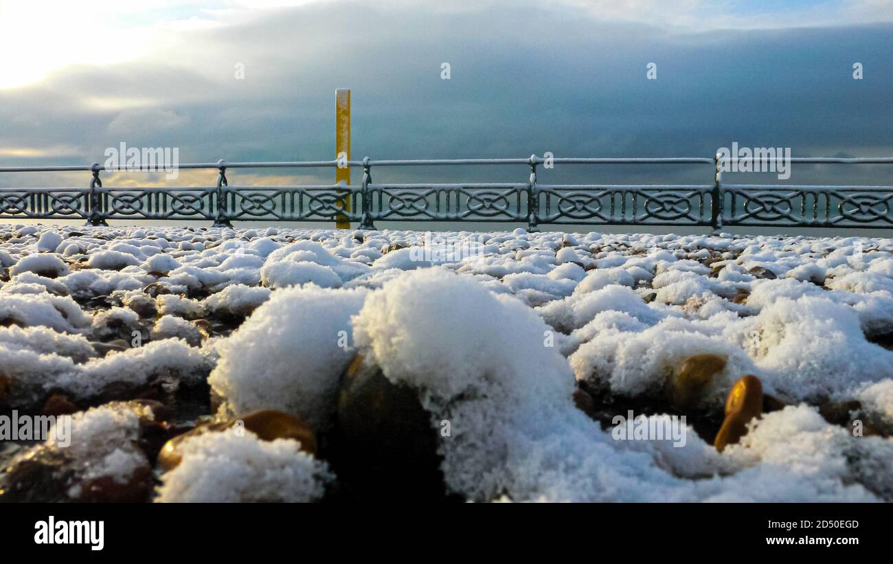 Snow covered pebble beach at sunrise on a frosty frozen winters morning ...