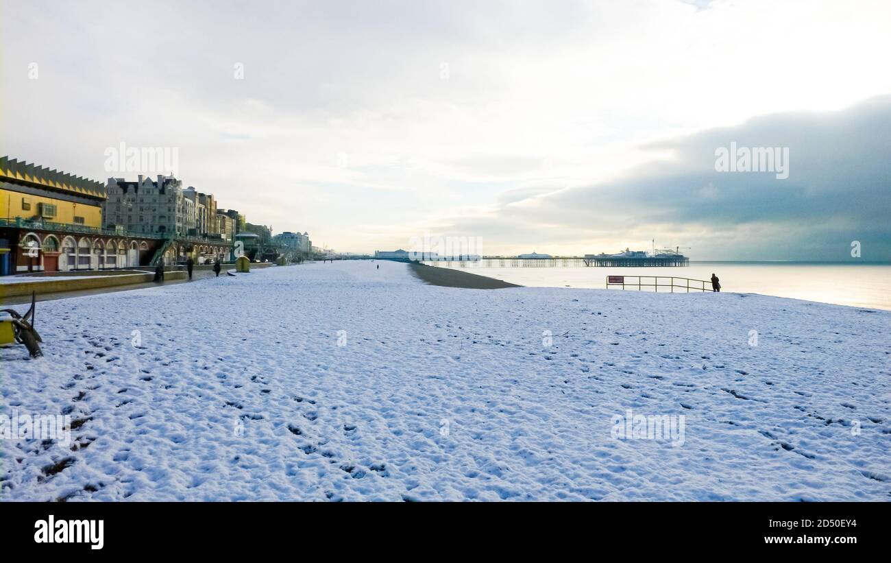 Snow covered pebble beach at sunrise on a frosty frozen winters morning ...