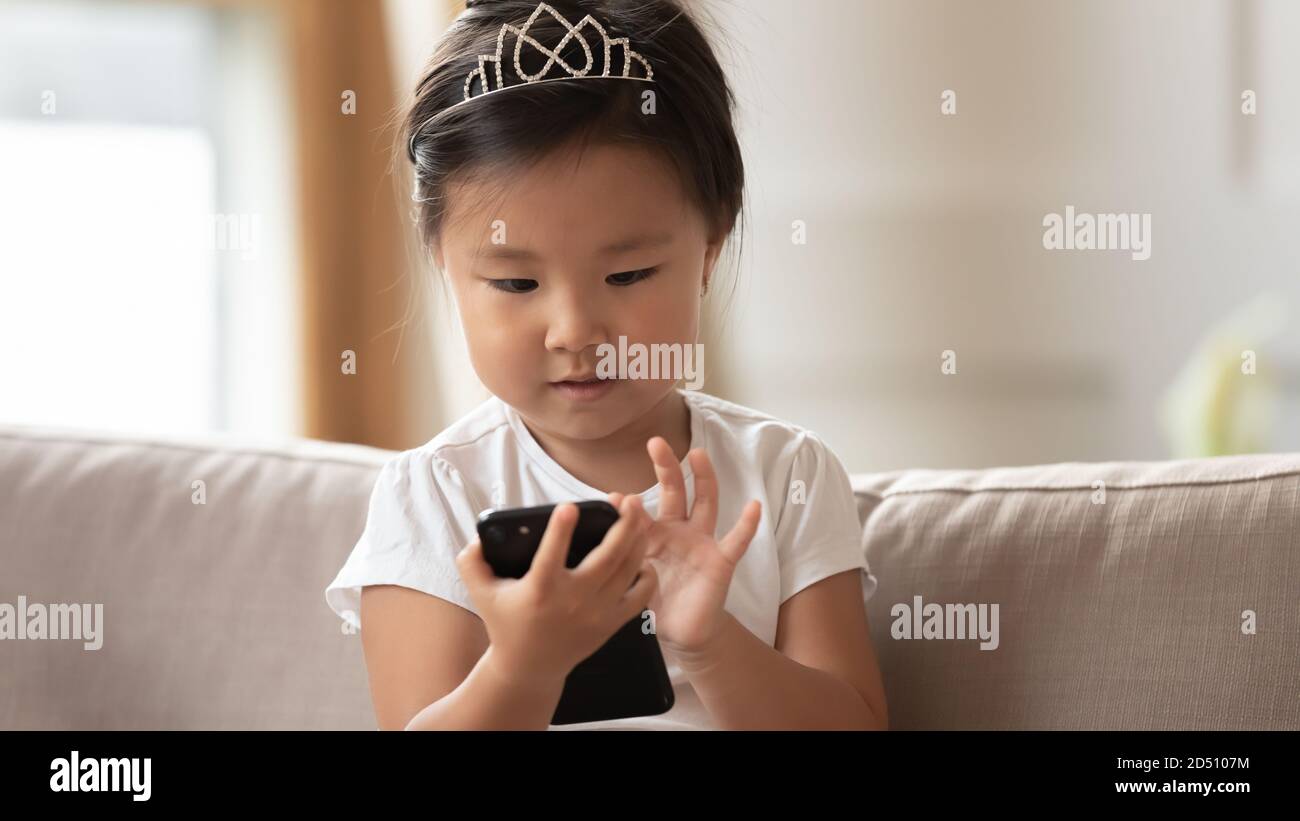 Close up cute little girl wearing princess diadem using smartphone ...