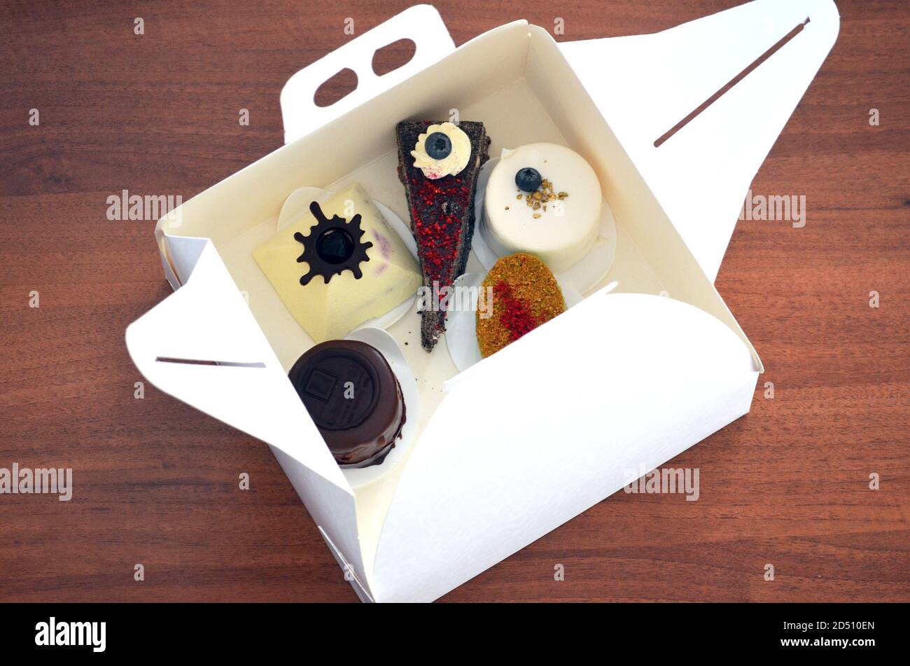 Elegant open white box full of various cakes and desserts on wooden ...