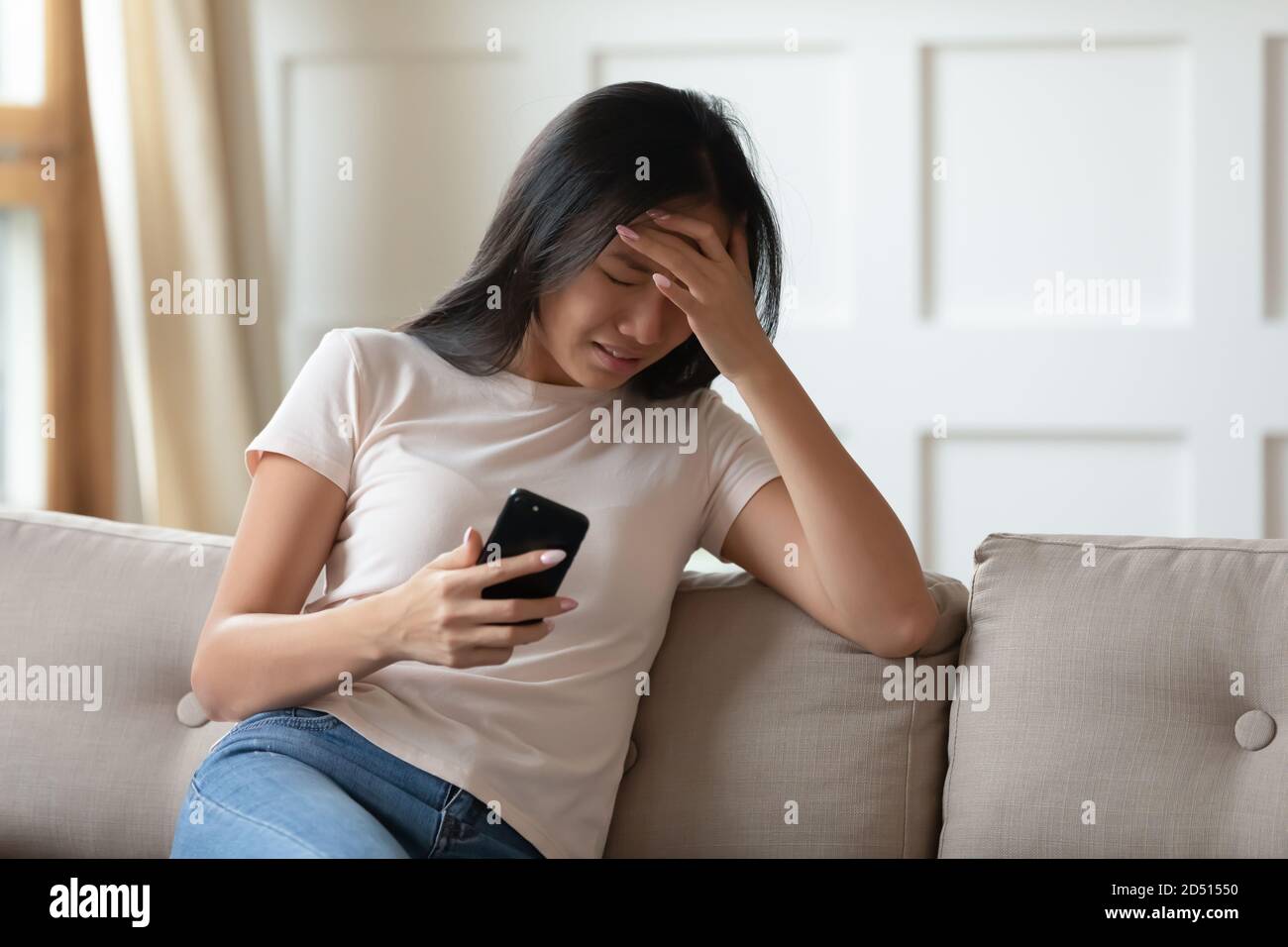 Upset young Asian woman crying, holding phone, received bad message ...