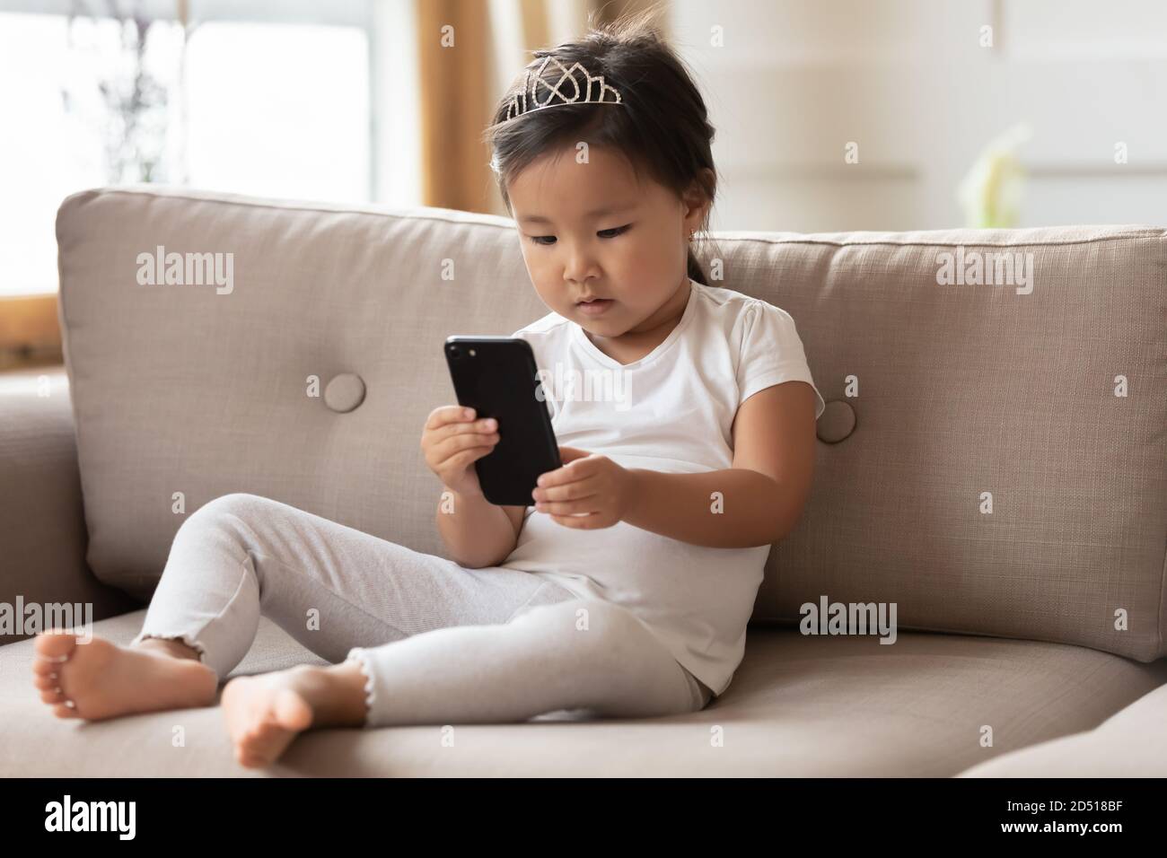 Cute little Asian girl wearing princess diadem using phone Stock Photo ...