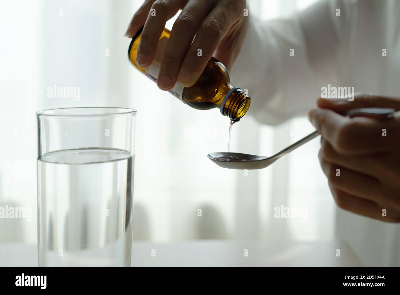 Woman hand pouring medication or cough syrup from bottle to spoon ...