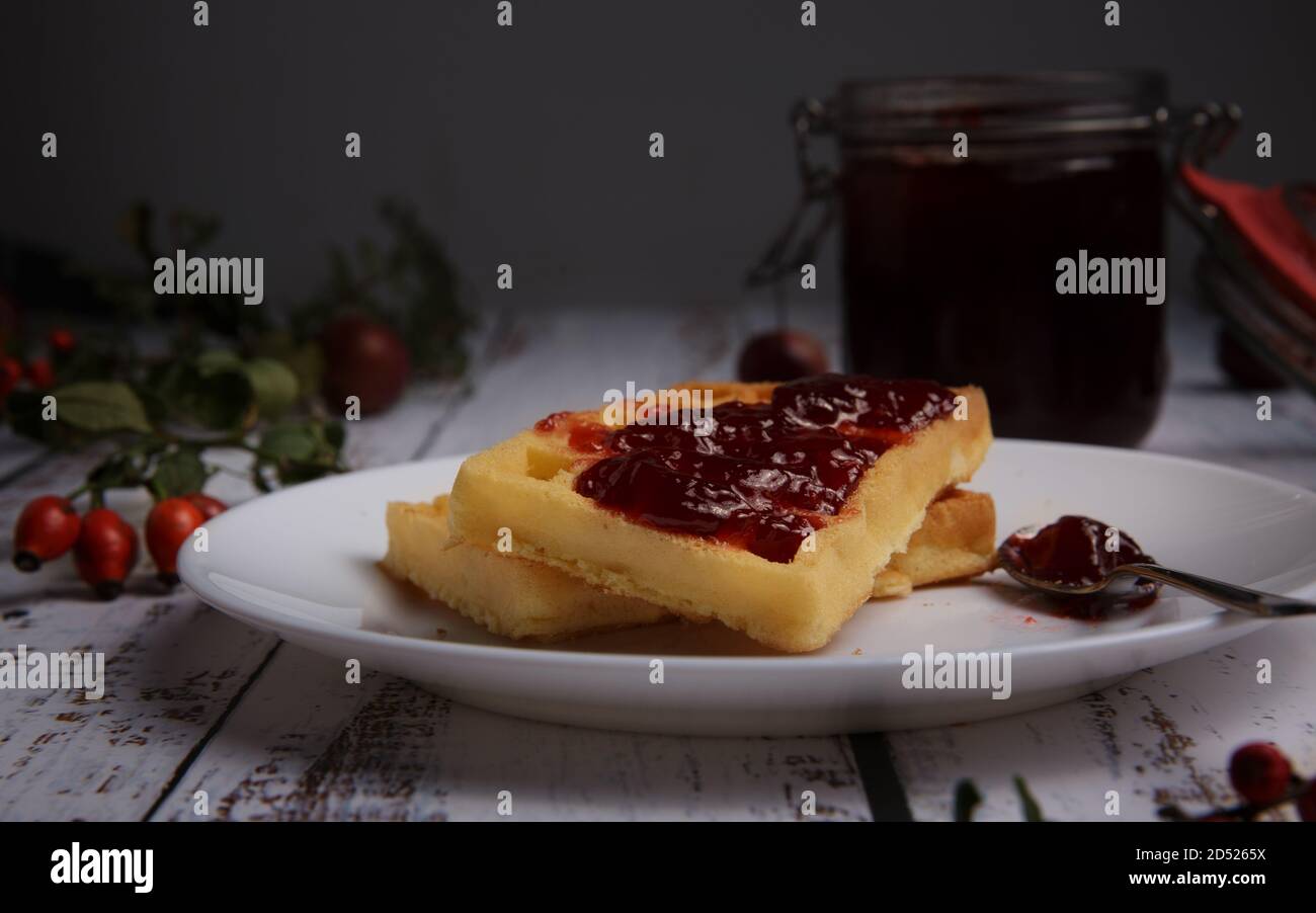 soft waffles smeared with strawberry jam and a glass jar with jam Stock ...