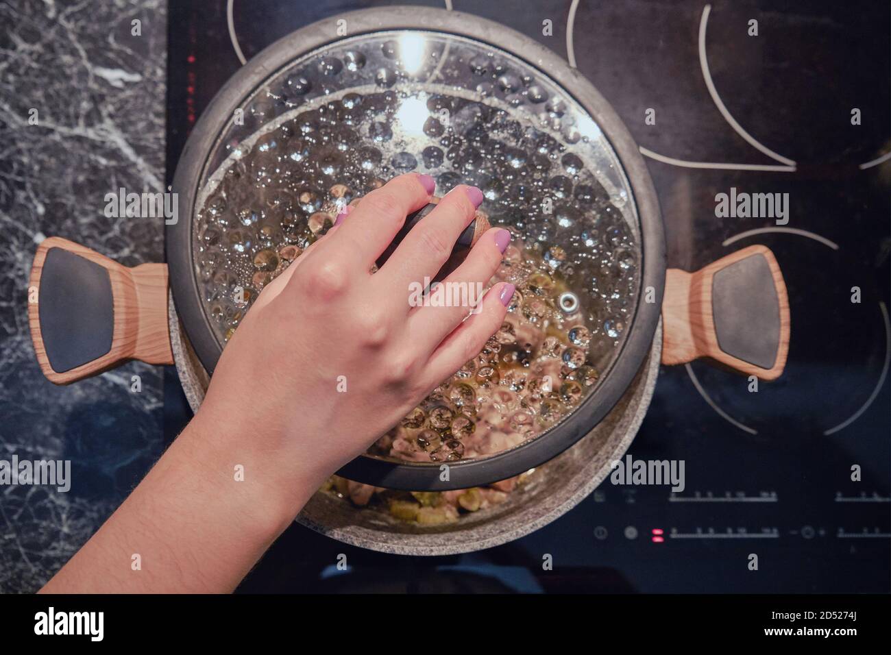 A woman hand opens the lid of a pot standing on an electric kitchen ...