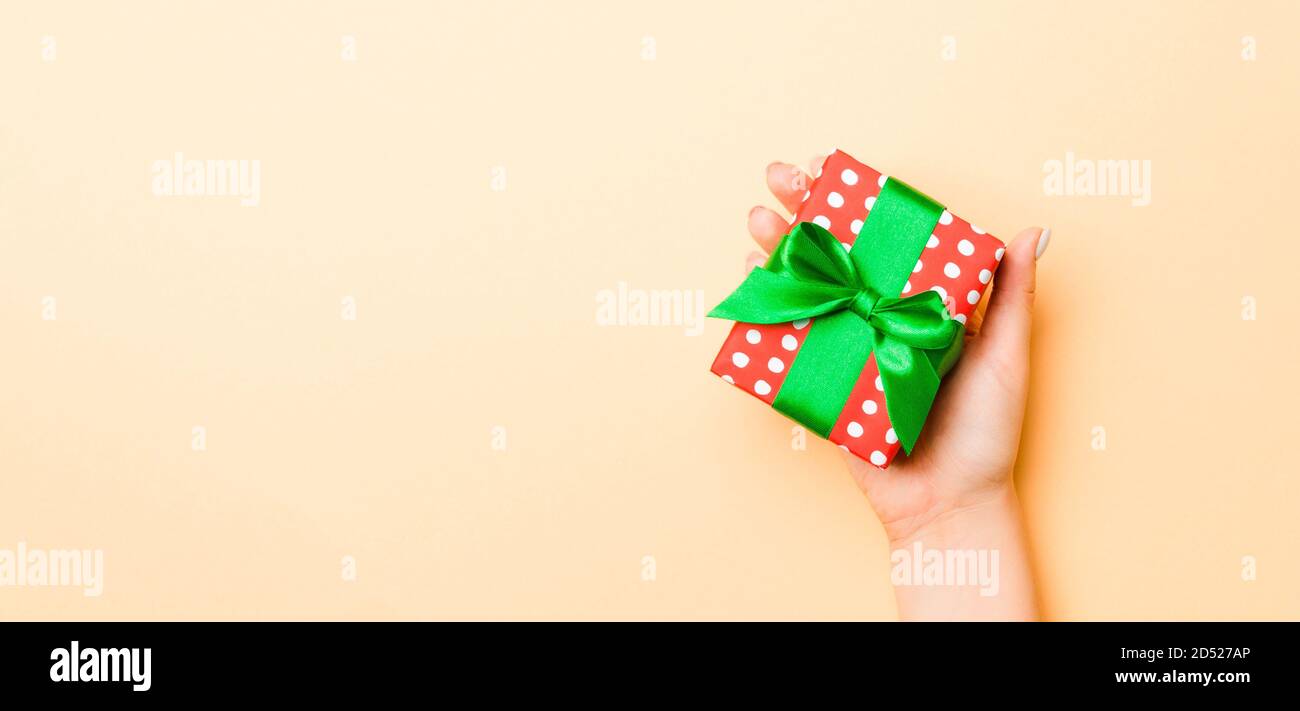 Flat lay of woman hands holding gift wrapped and decorated with bow on ...
