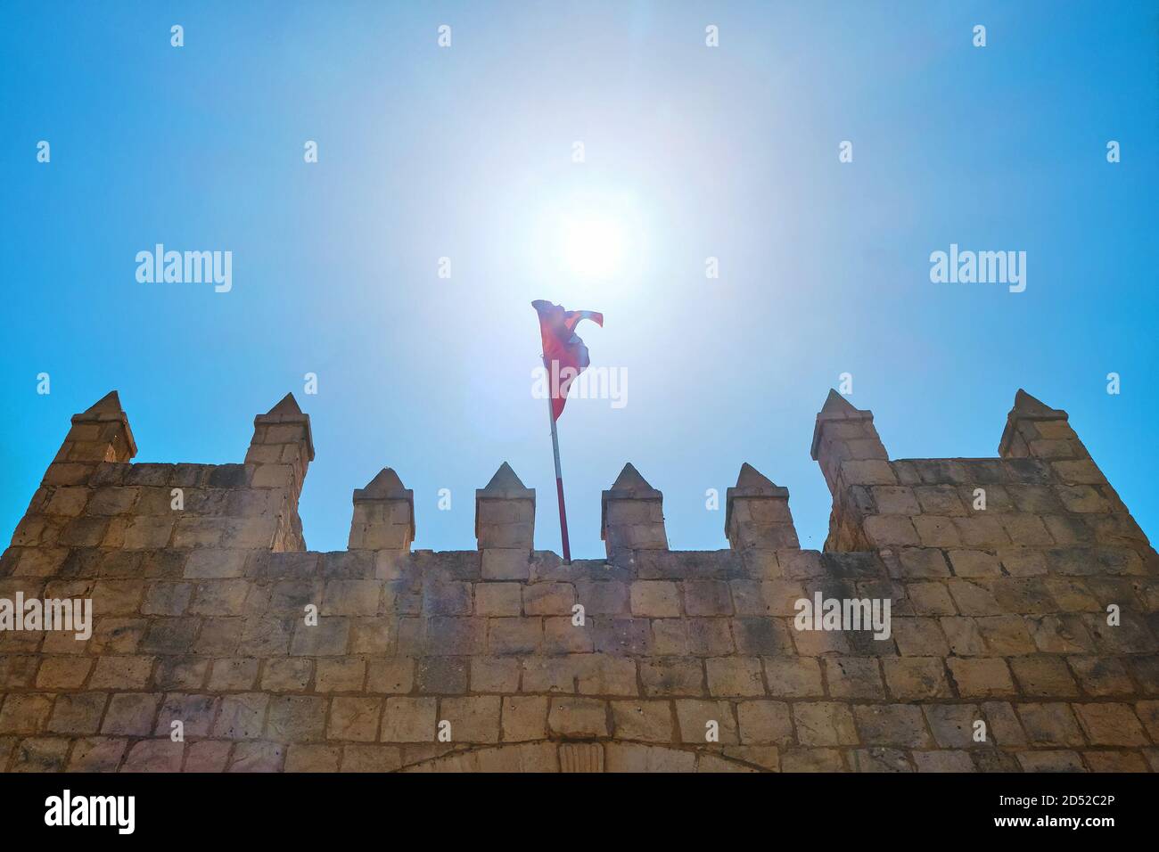 The flag flies over the fortress wall against the sky and the sun ...