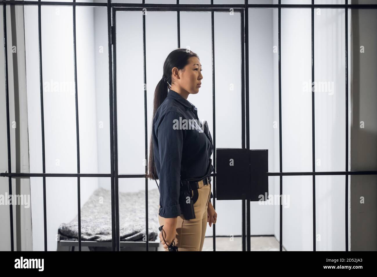 A young prison guard poses in front of prison bars in uniform. In a ...