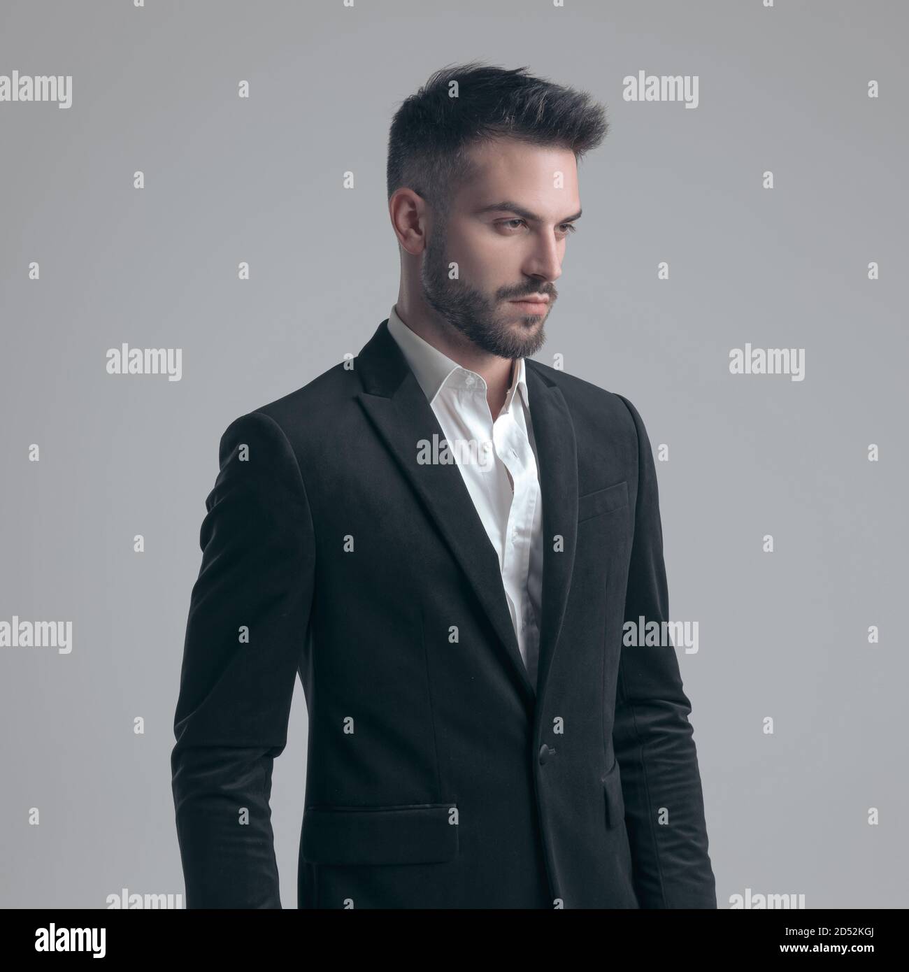 Serious elegant man looking away and wearing suit while walking on gray ...