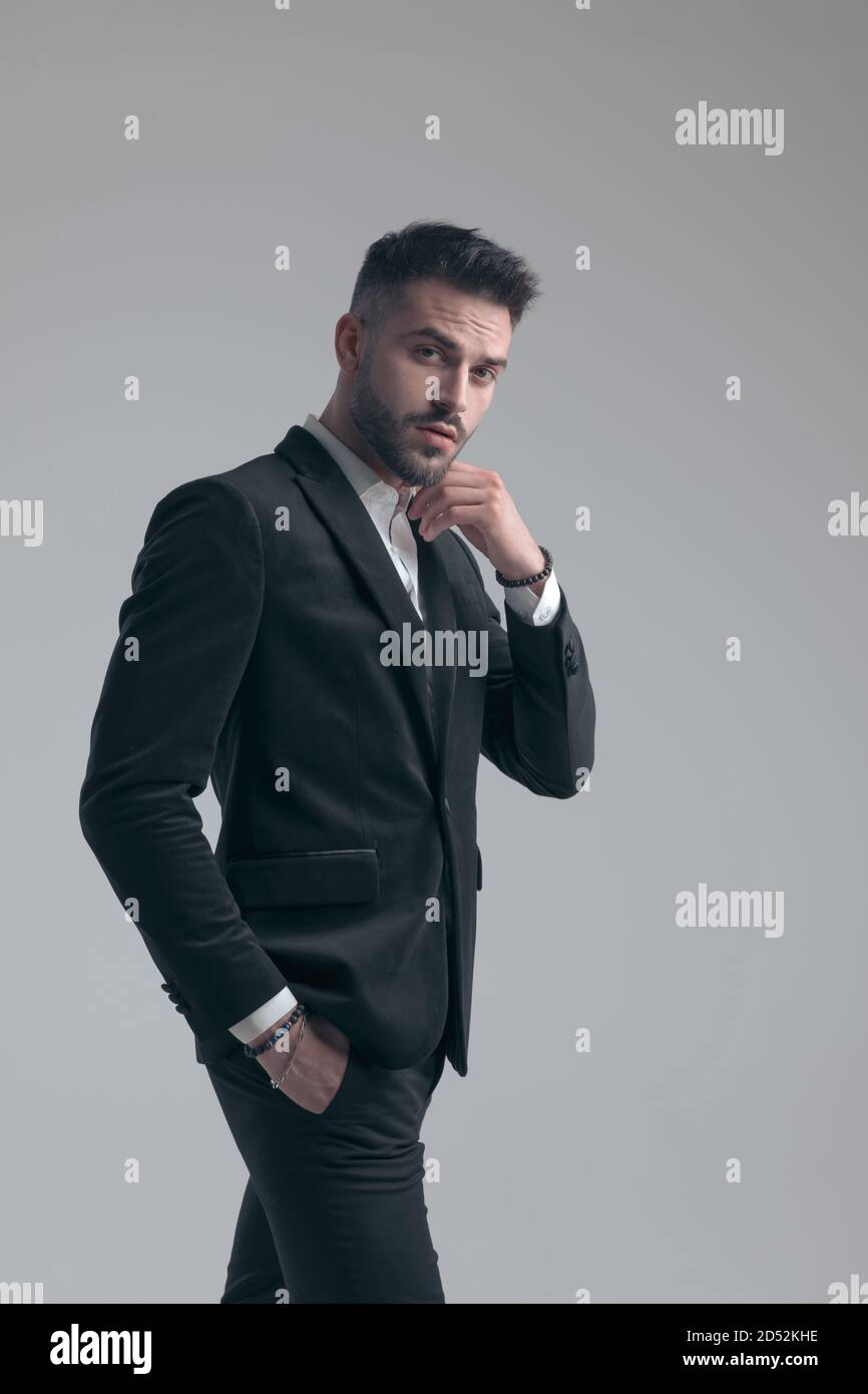 Charming elegant man fixing his collar with hand in pocket, wearing ...