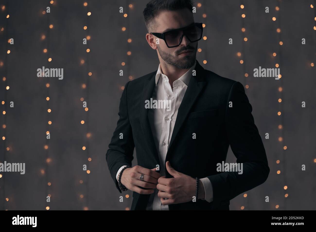 Determined fashion model adjusting his jacket and looking away while ...