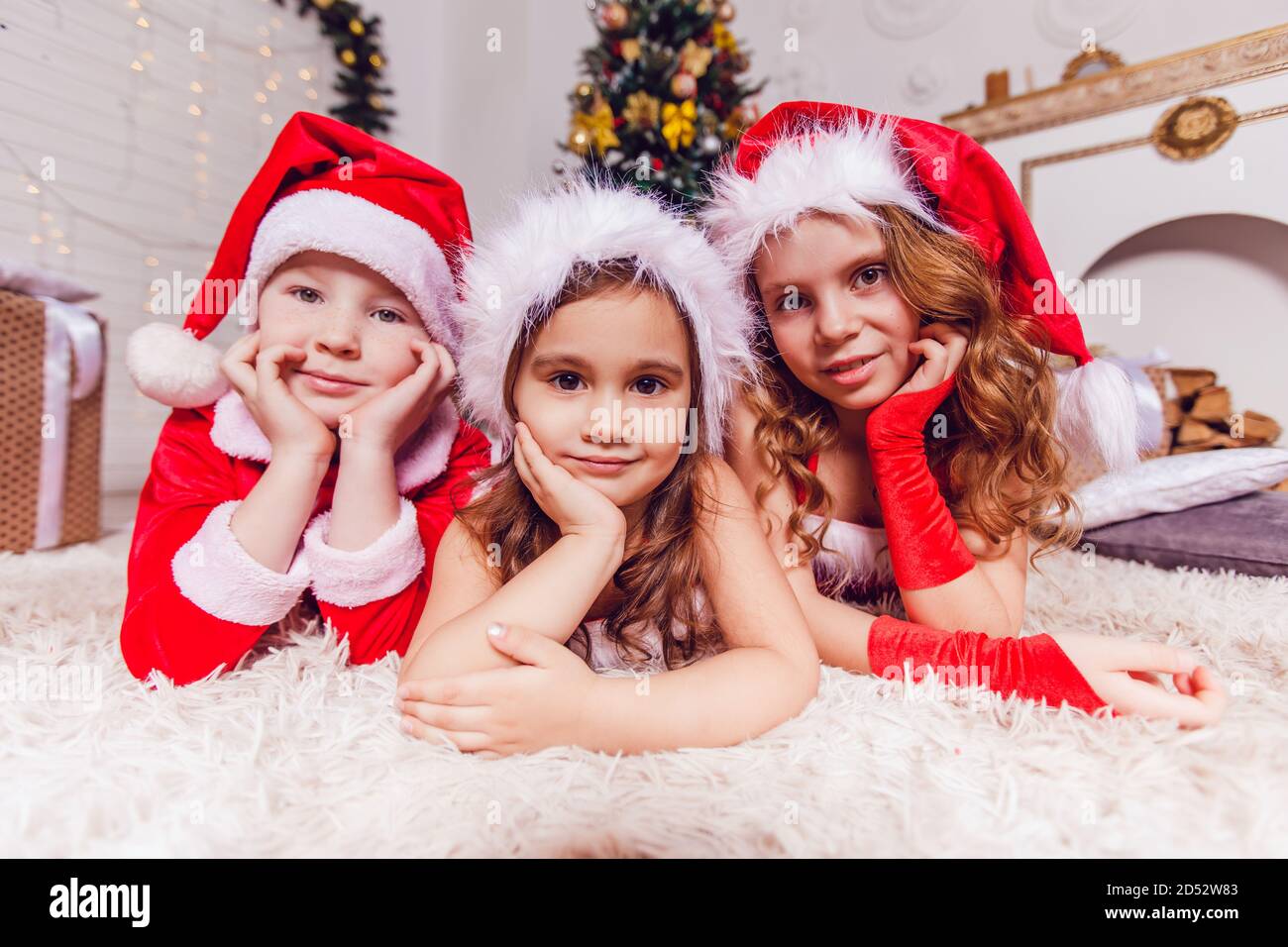 Children in red santa claus costumes lie near the christmas tree Stock ...