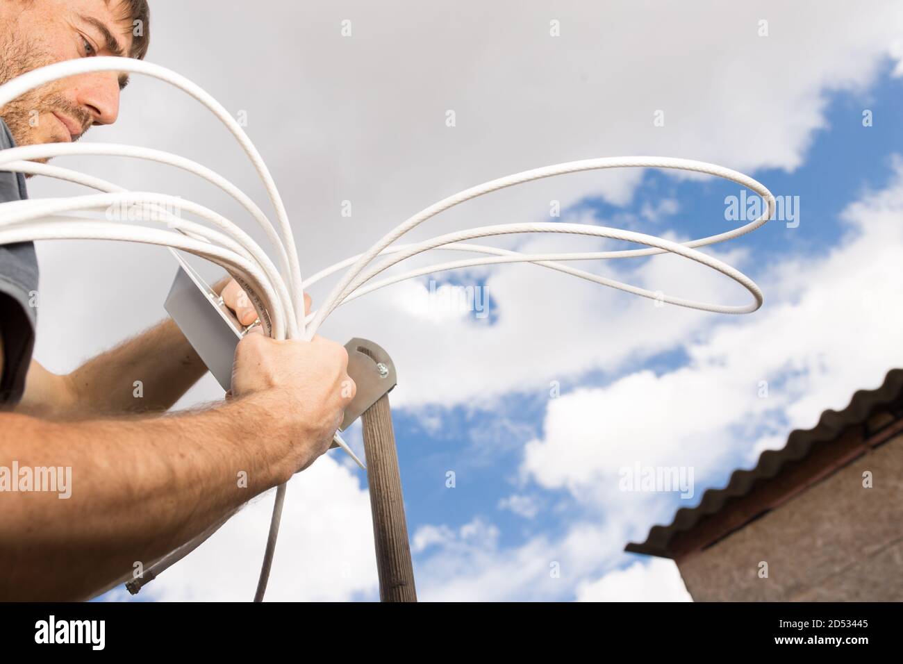 A young man works with a cable and an antenna installation outside ...