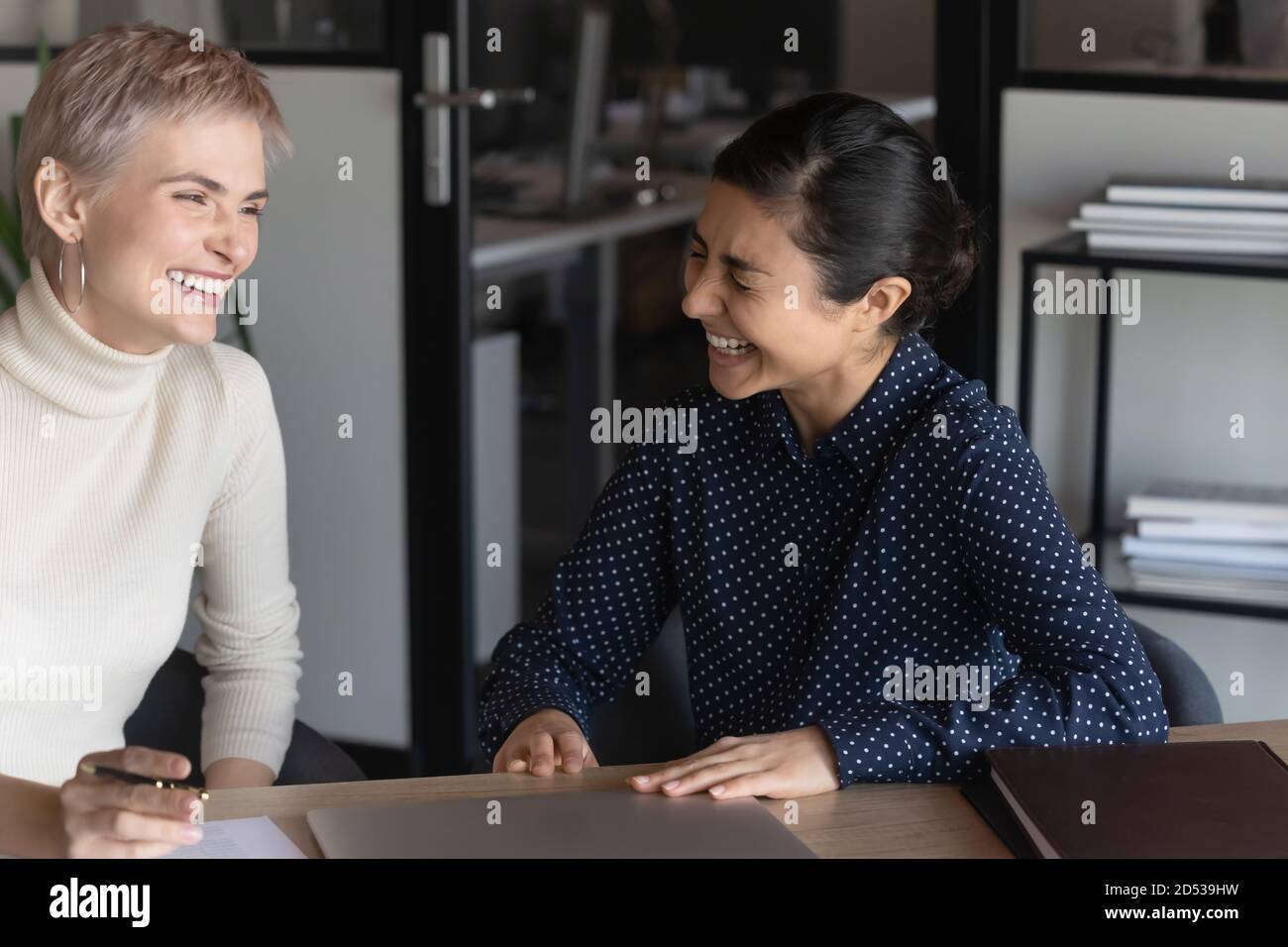 Overjoyed multiracial female colleagues laugh at workplace Stock Photo ...