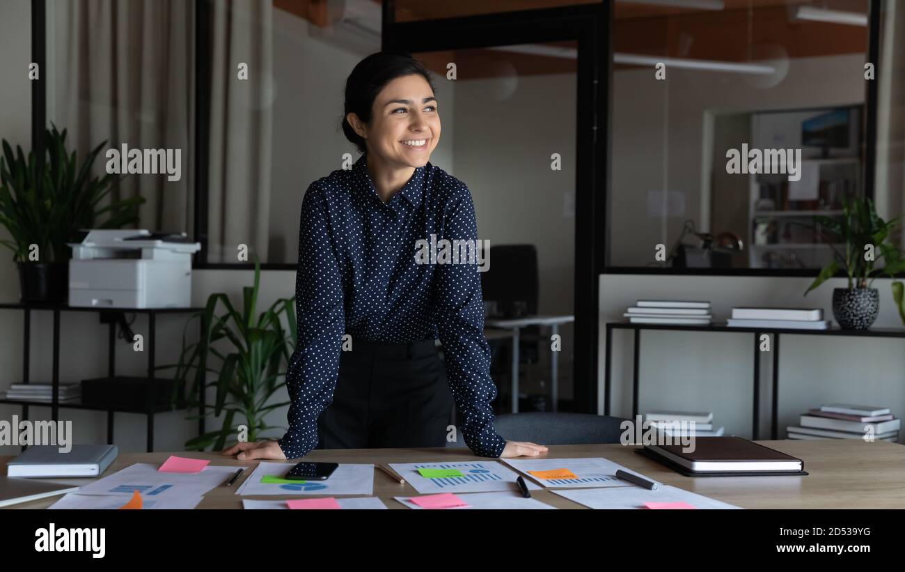 Smiling indian female employee look in distance dreaming Stock Photo ...