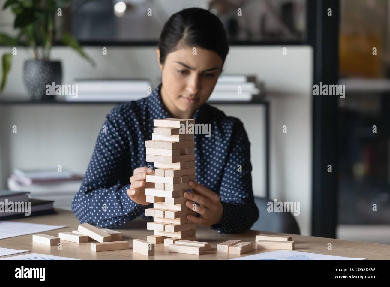 Pensive indian female employee play wooden stack game Stock Photo - Alamy