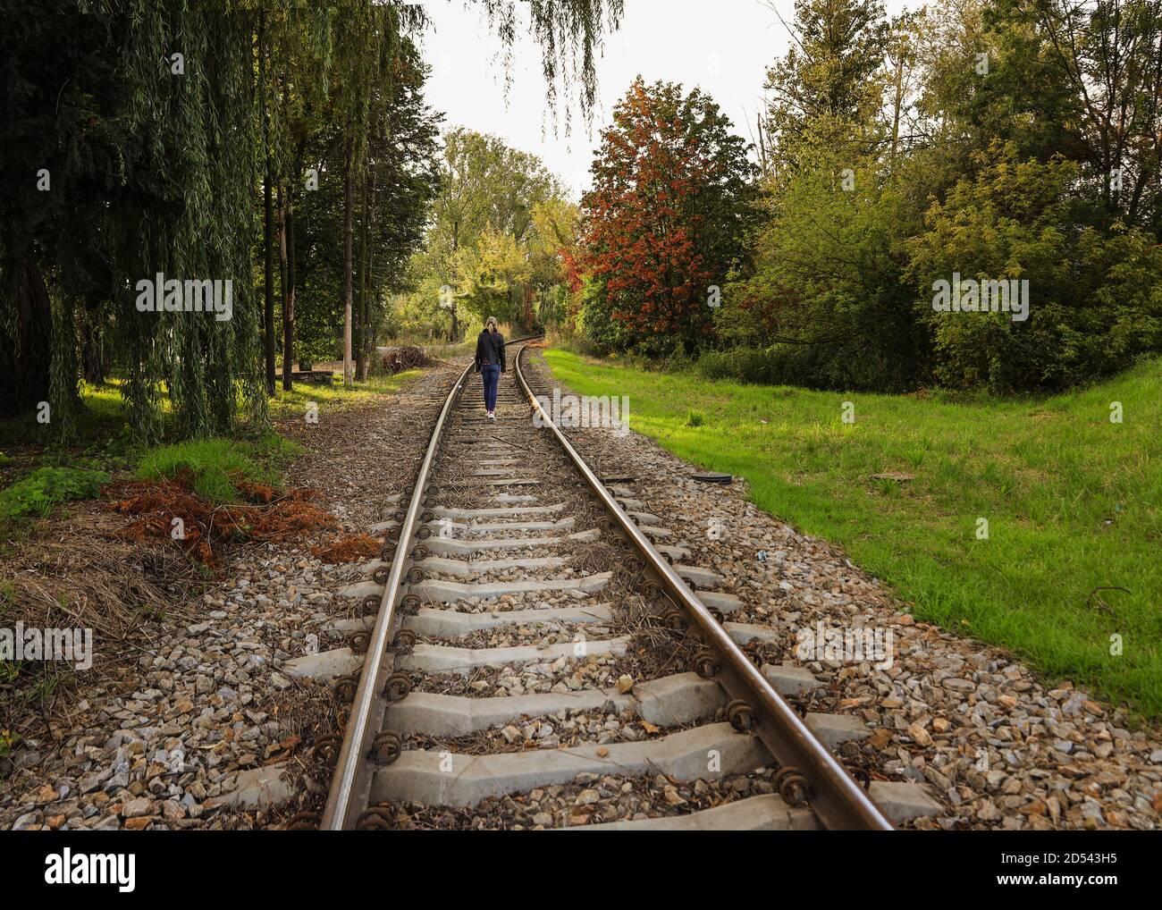 the girl walks along the railway track and there are green trees around ...