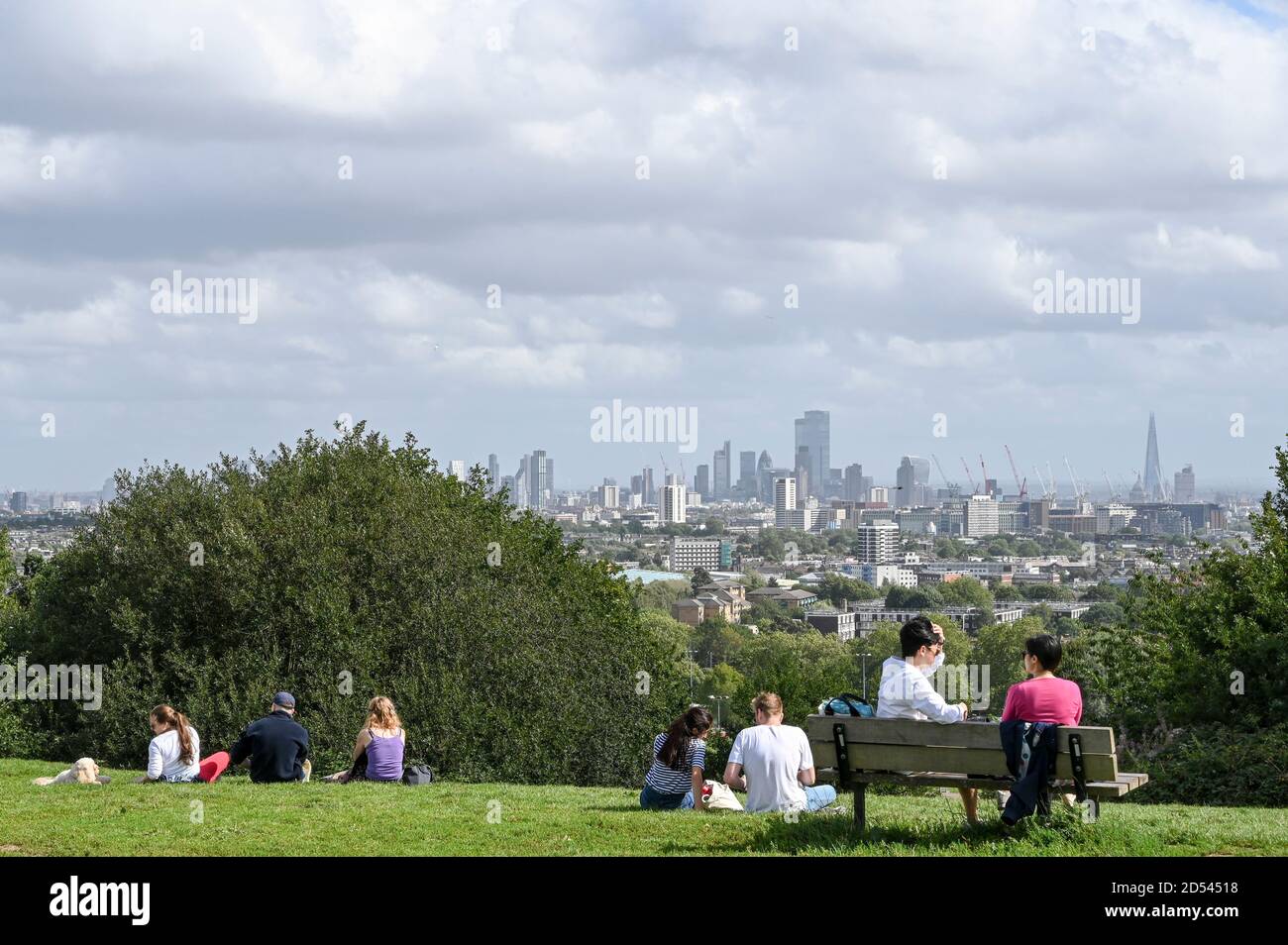 People chatting in small groups on Parliament Hill, London UK, with a ...