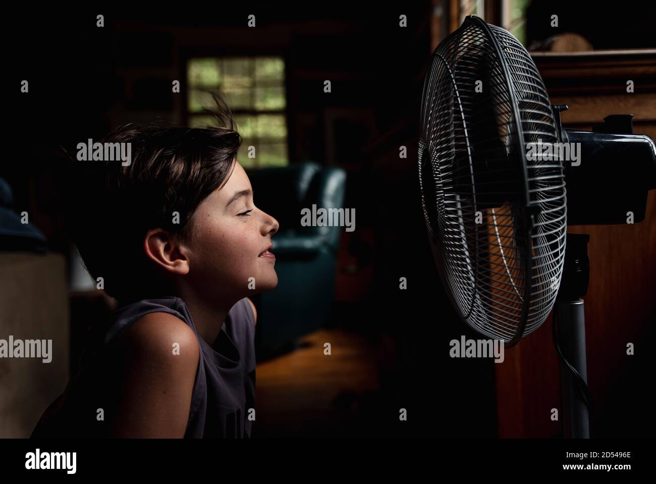 Young boy cooling off in front of an electric fan in dark room Stock ...