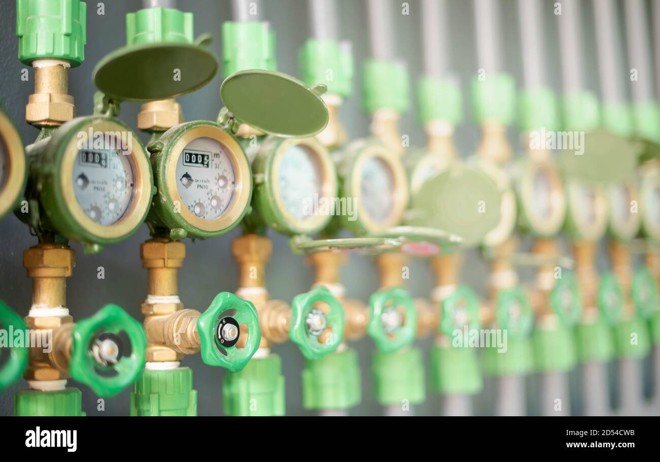Row of industrial pipelines and valves with green wheels on grey wall ...