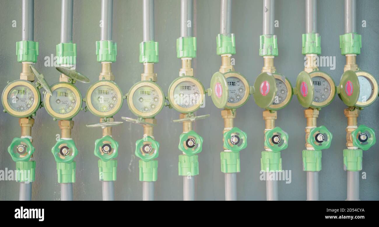 Row of industrial pipelines and valves with green wheels on grey wall ...