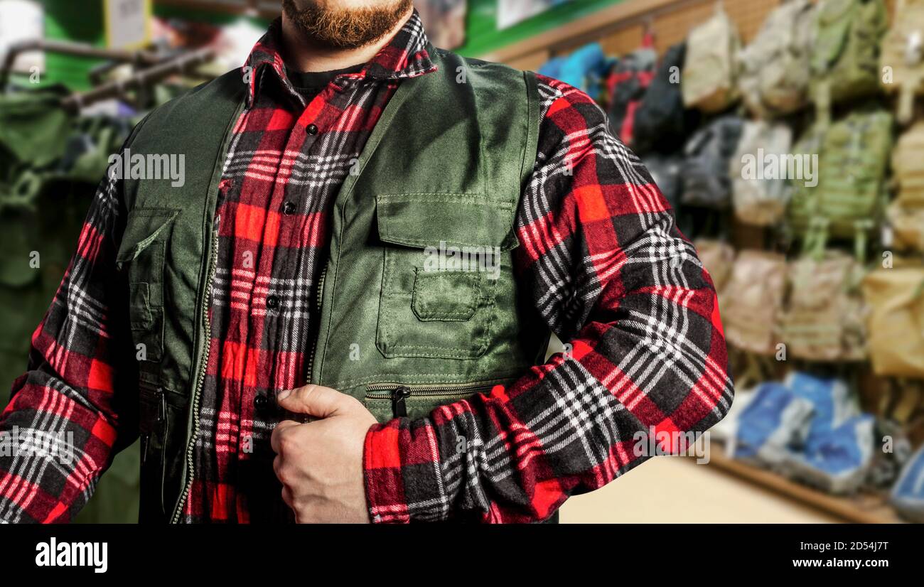 Photo of a bearded man in uniform store putting on khaki hunting jacket ...