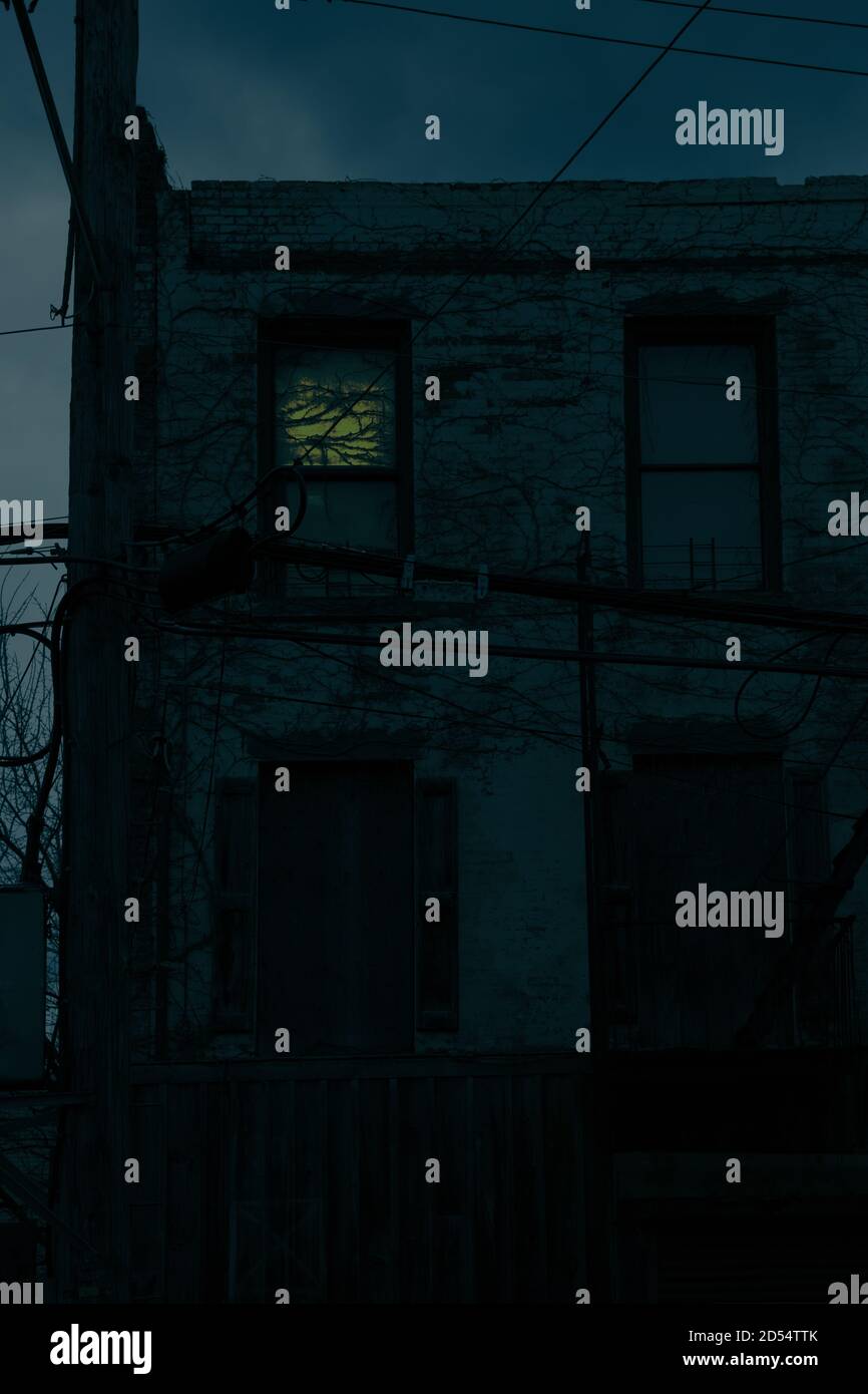Old house on a stormy evening with one light in window and overhead ...