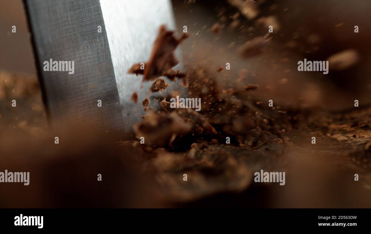 Detail of chisel cutting off raw chocolate, freeze motion of flying ...