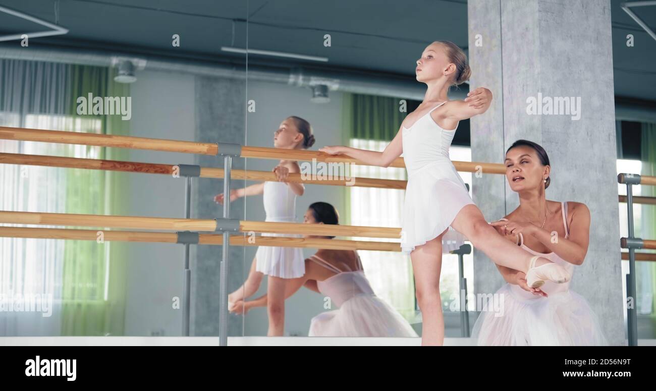 Woman teacher helps little girl ballerina to do exercises raise leg in ...