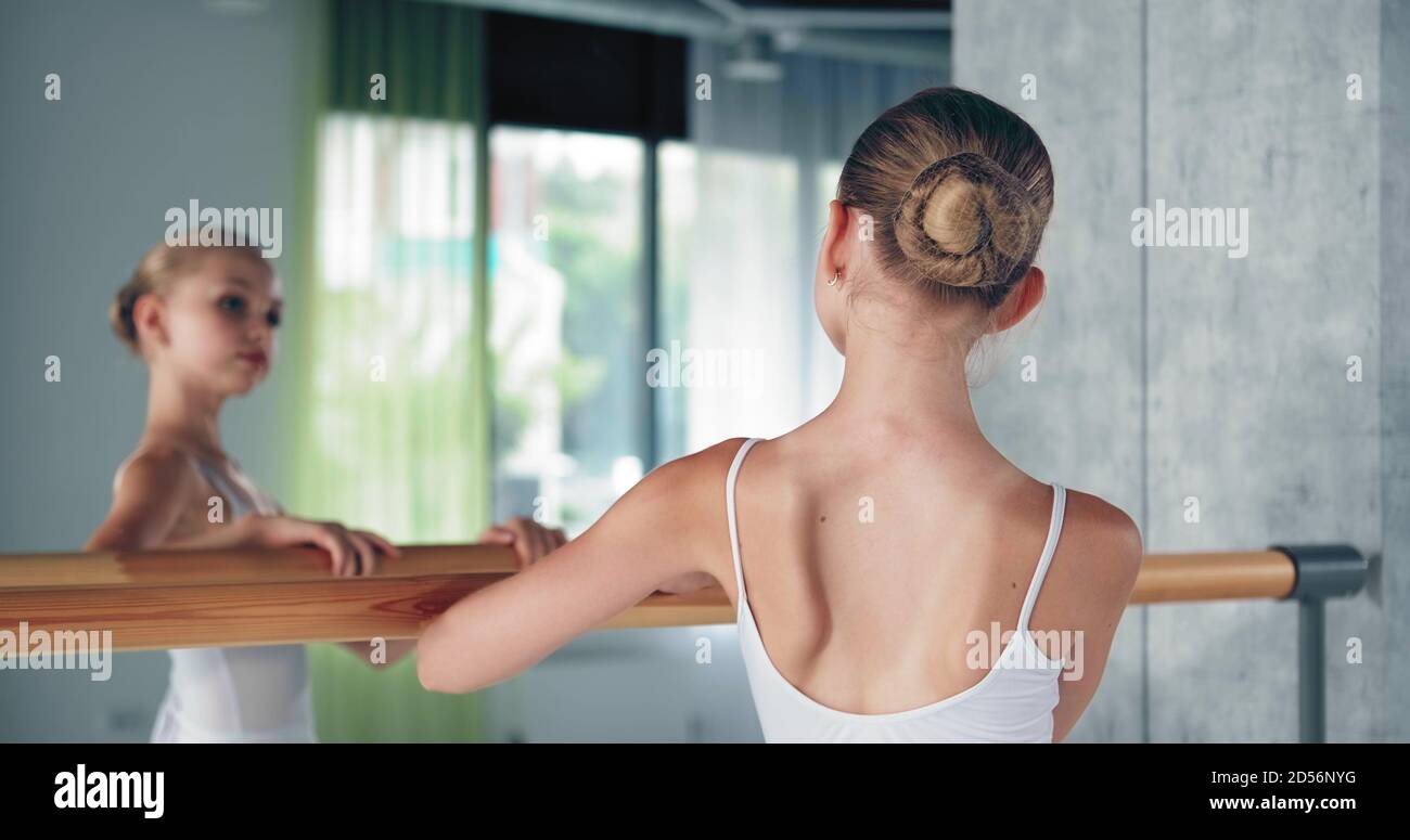 Cute preteen girl ballerina with bun in white costume looks into large ...
