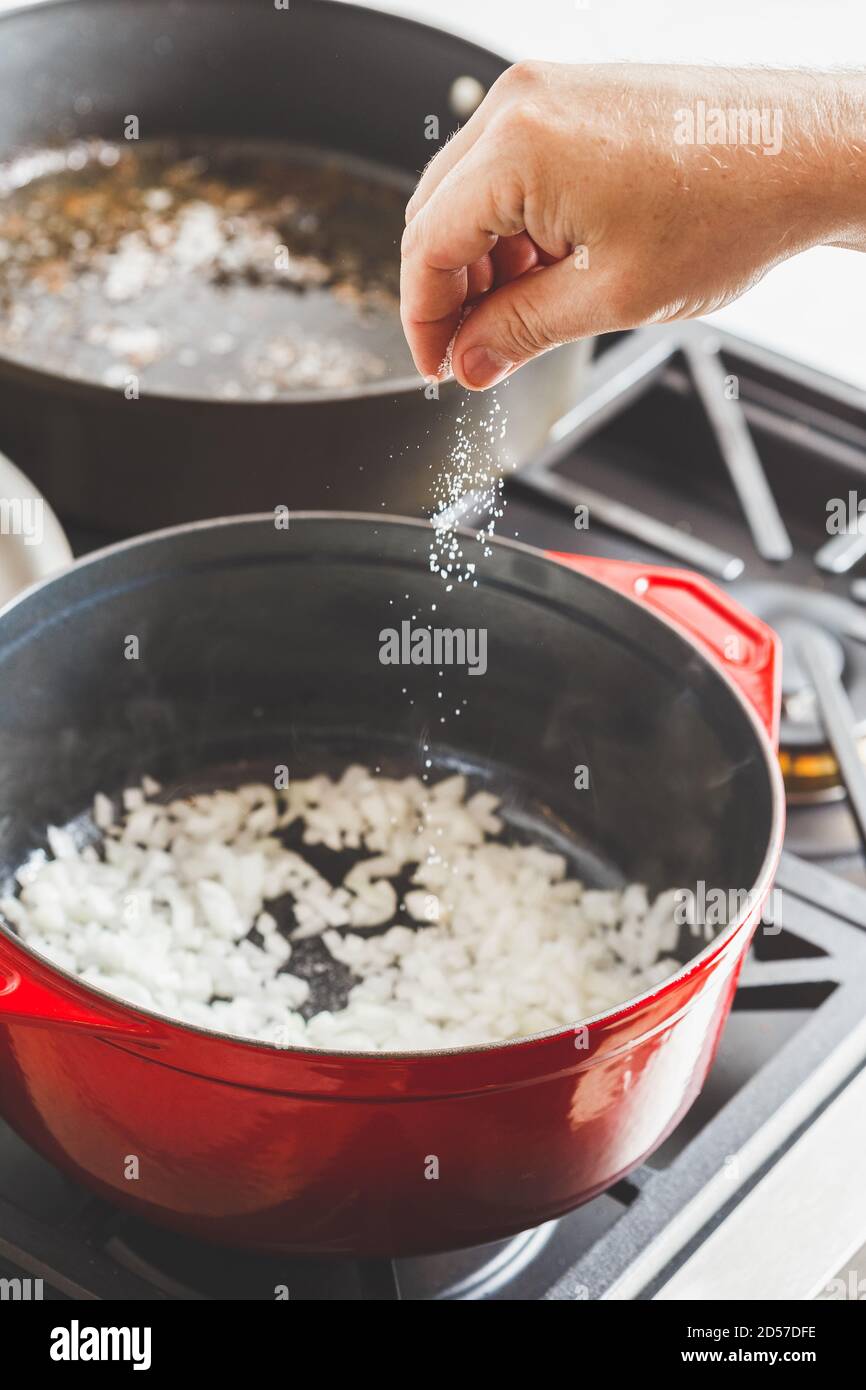 Man's hand adding salt while cooking white onion finely chopped a red ...