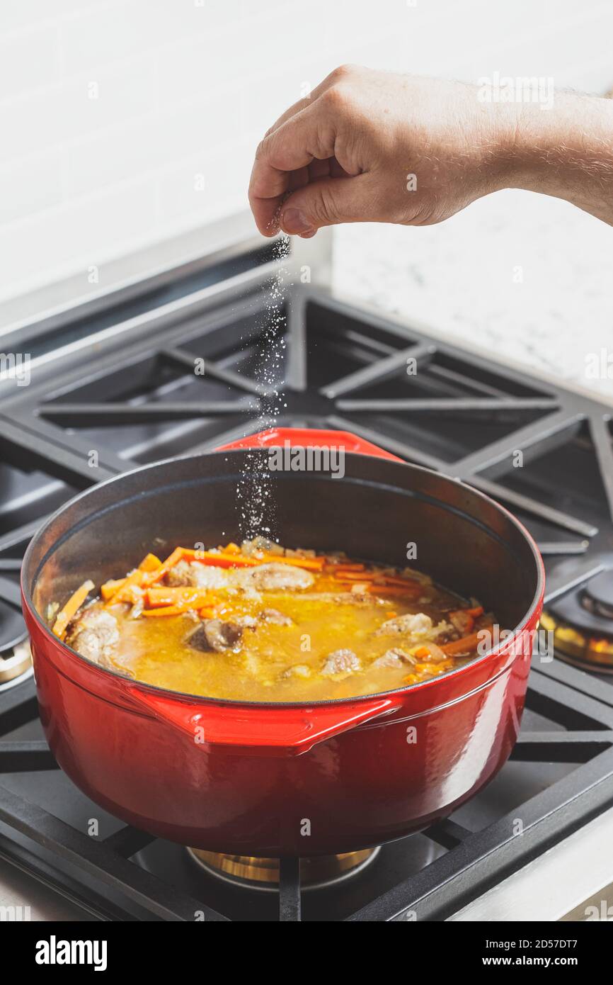 Adding salt to Pilaf being cooked at home in a red cast iron french ...