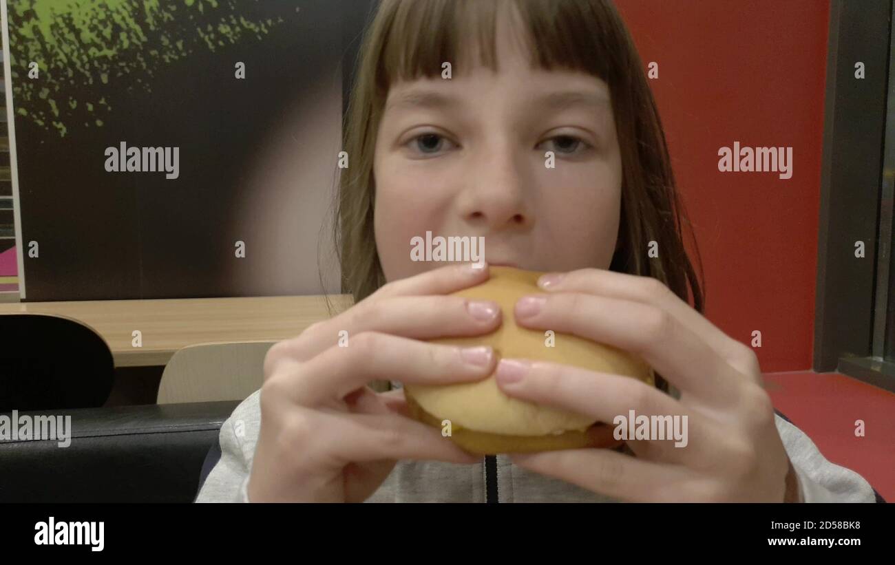 Young happy teenager eating tasty hamburger in fast food restaurant ...