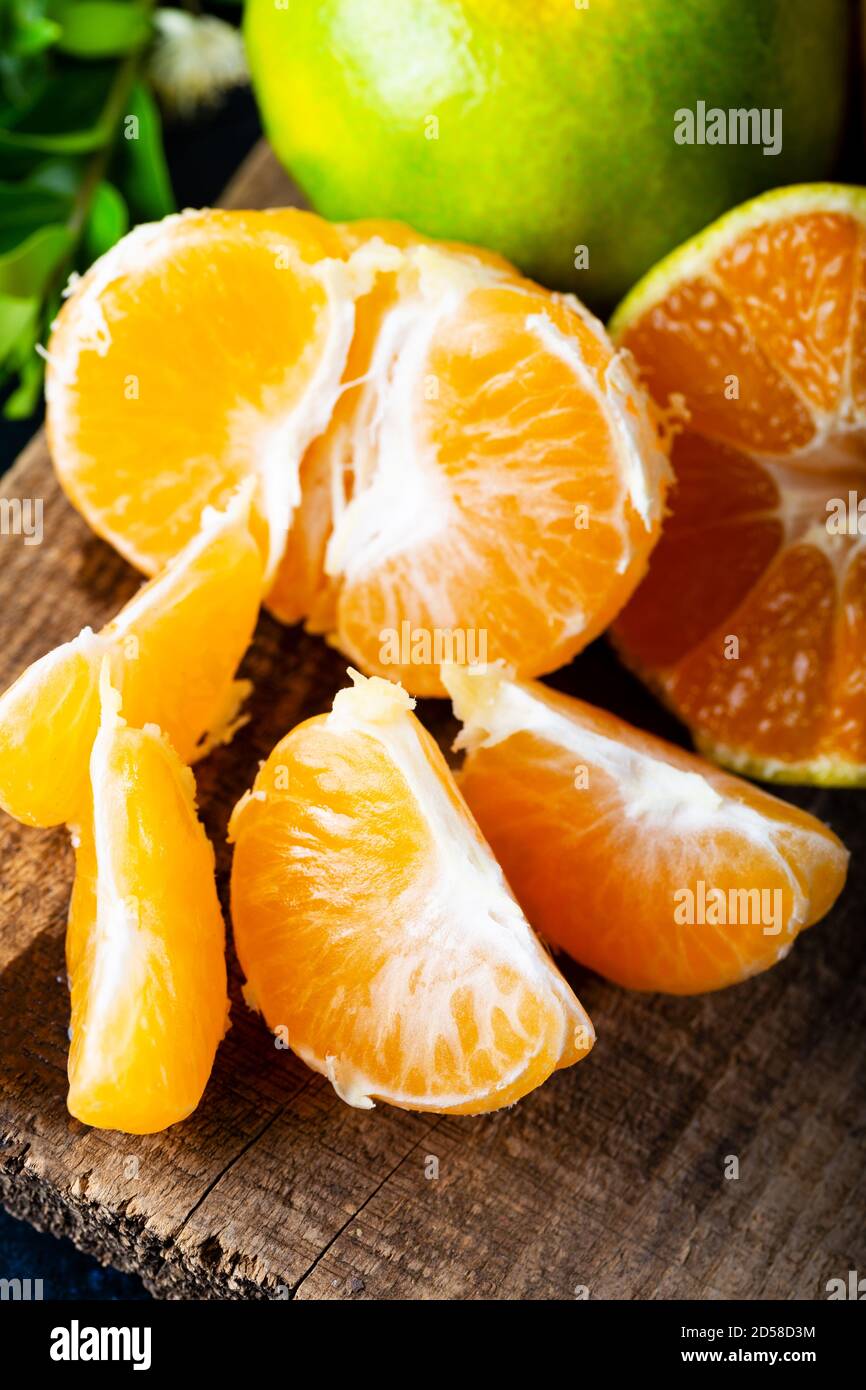 Ripe Mandarin fruit peeled open and place on old rustic look timber ...