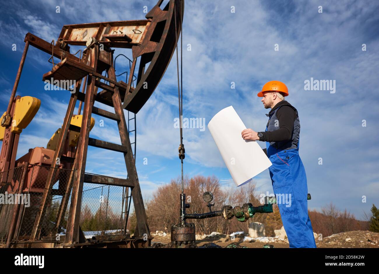 Side view of oil worker holding plan of oil field at petroleum pump ...