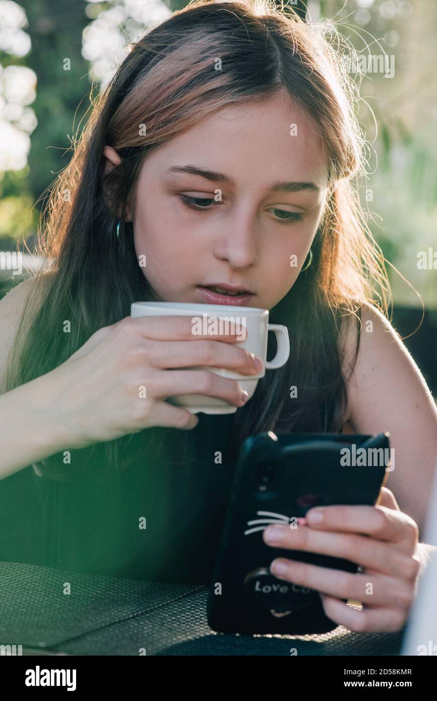 Teenage girl using her cell phone, while having a cup of tea. Teenage ...