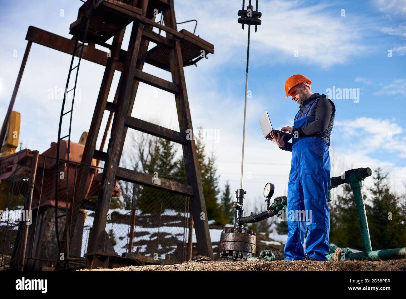 Oil engineer, wearing blue overalls and orange helmet, with a laptop ...