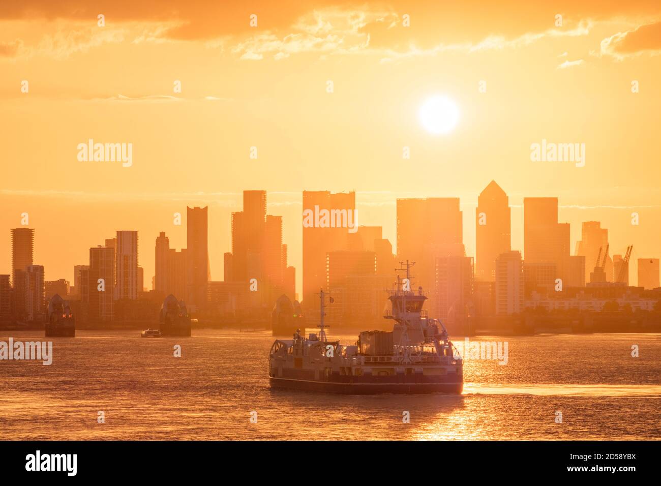 Woolwich Ferry sailing past Thames Barrier and Canary Wharf at dusk ...