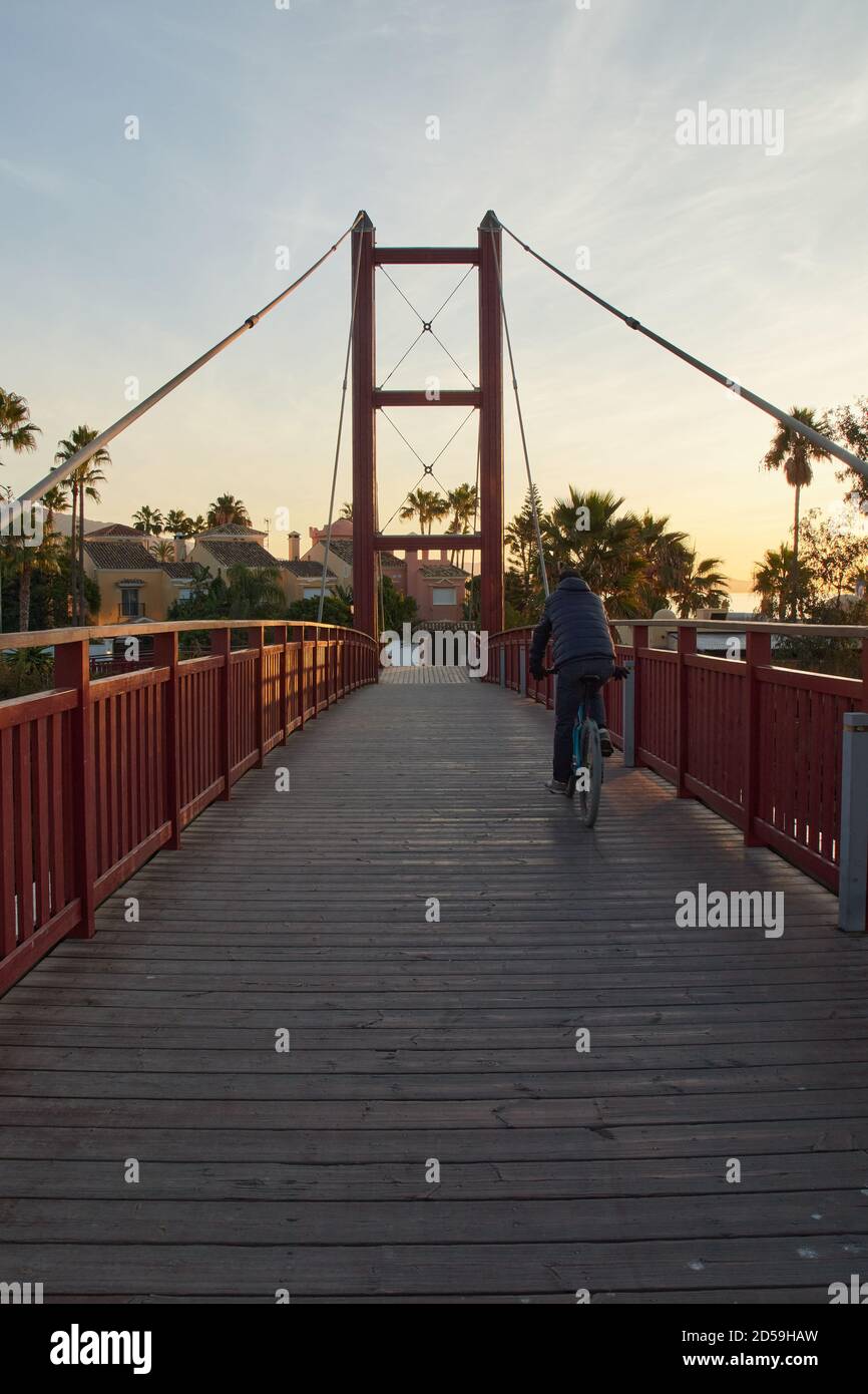 Rear view of man riding bicycle on bridge in city over a wood bridge at ...