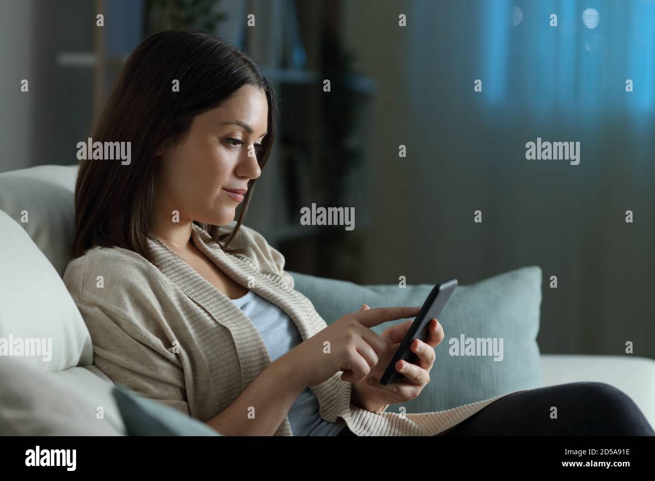 Woman using smart phone sitting on a sofa in the night at home Stock ...